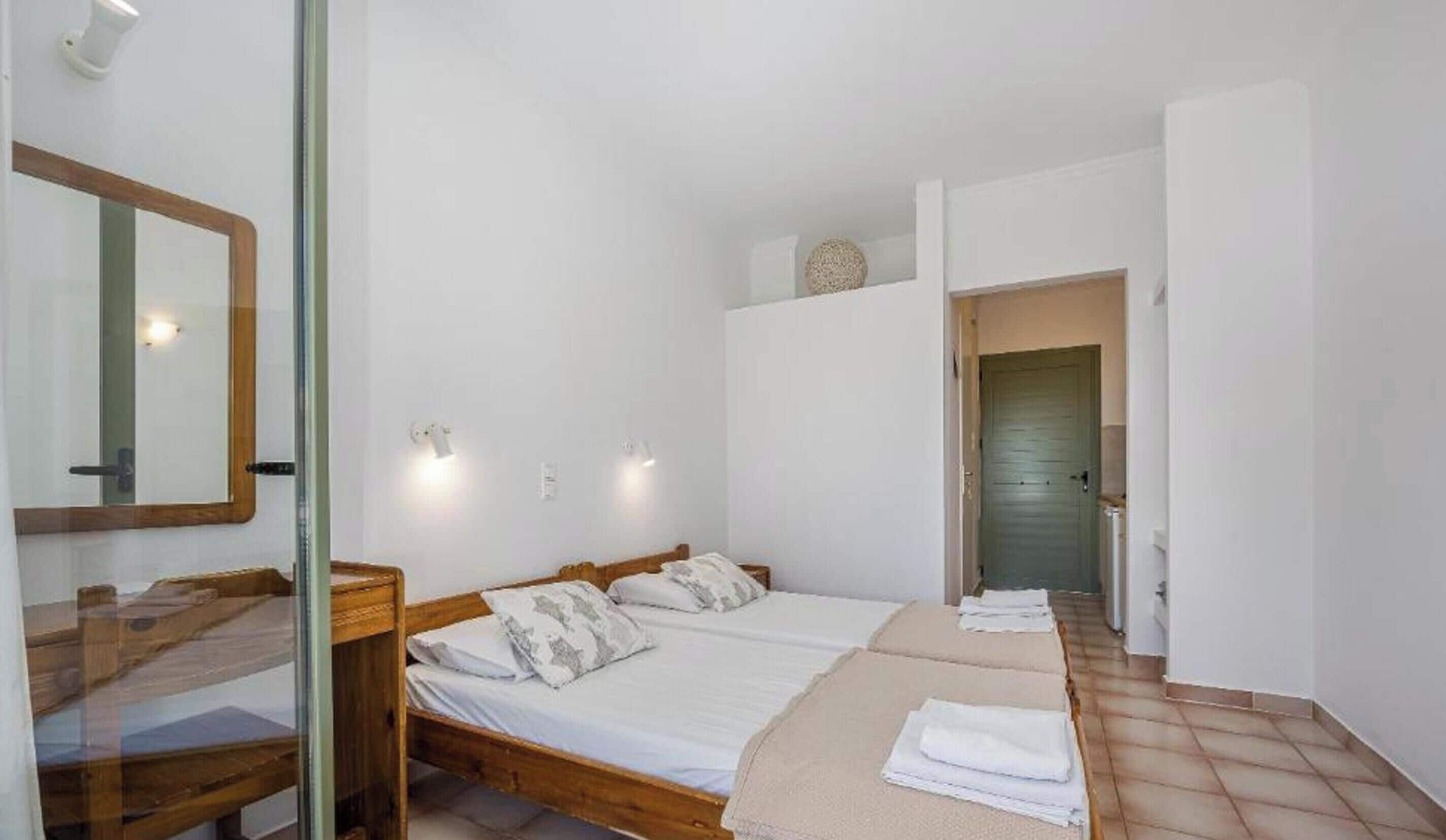 Quarto com uma cama, mesas de cabeceira, um espelho e uma porta que dá para outro cômodo.