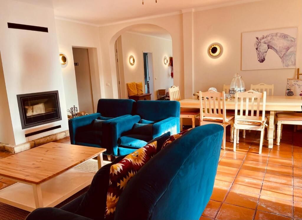 Sala de estar com lareira, sofá azul, mesa de jantar de madeira e cadeiras brancas.