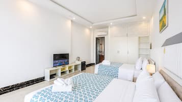 Quarto de hotel com duas camas, televisão, pequena cozinha e banheiro.