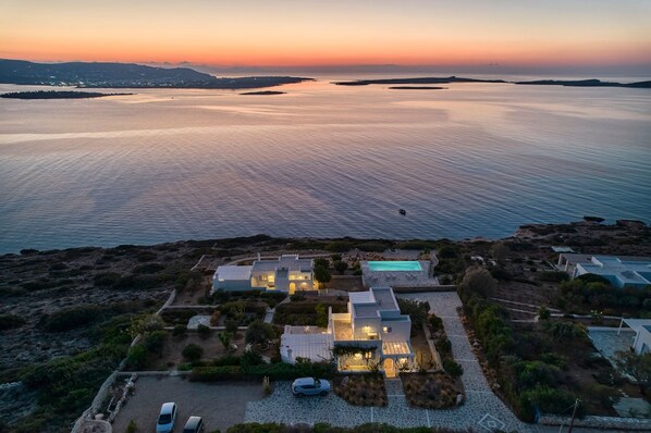 Vista aérea de uma propriedade costeira com vários edifícios, uma piscina e um estacionamento.