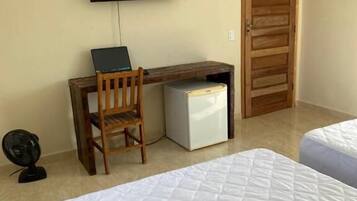 Um quarto com cama, escrivaninha com cadeira, televisão, frigorífico e porta de madeira.
