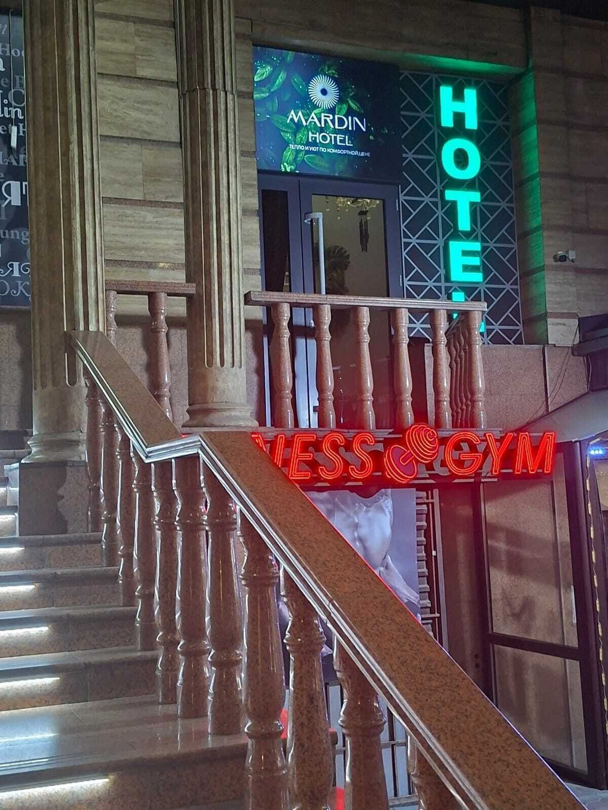Entrada de hotel com um letreiro de neon para 'MARDIN HOTEL' e uma placa indicando academia.