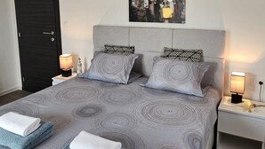 Quarto moderno com uma cama grande, duas mesas de cabeceira, uma porta preta e uma pintura com vista para a cidade na parede.
