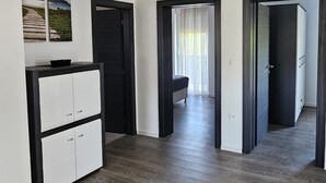 Um corredor com piso de madeira, um guarda-roupa preto e uma cama com janela ao fundo.