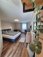 Quarto moderno com cama, mesa de cabeceira, escrivaninha, cadeira e uma planta.