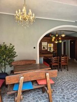 Uma sala de jantar com um candelabro, bancos de madeira e piso de pedra.