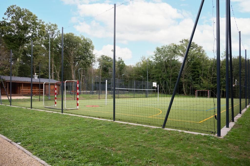Um campo de esportes com um gol, cercado por uma grade, e um edifício ao fundo.