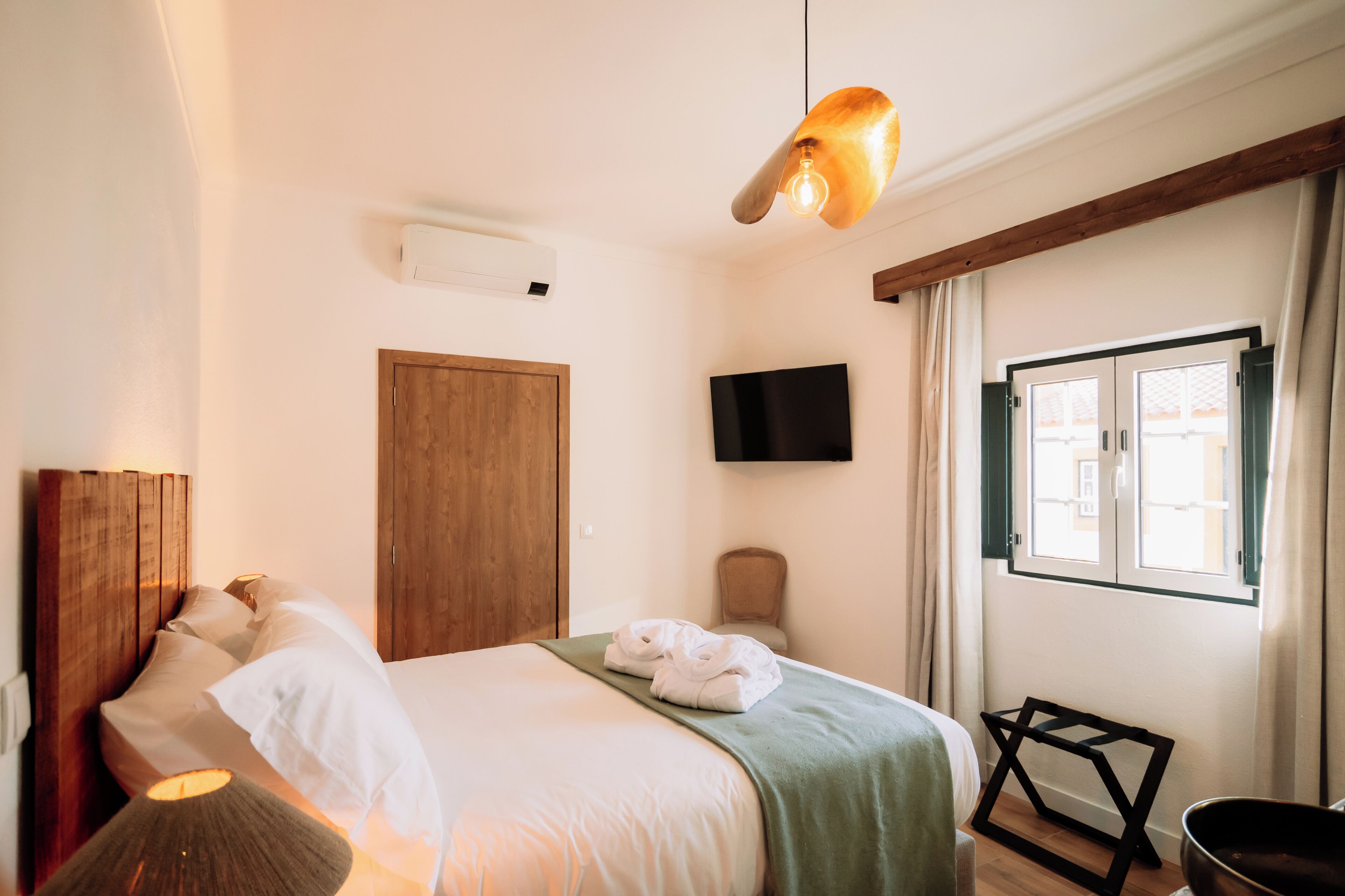 Quarto de hotel com uma cama, televisão de tela plana, porta de madeira e janela com cortinas.