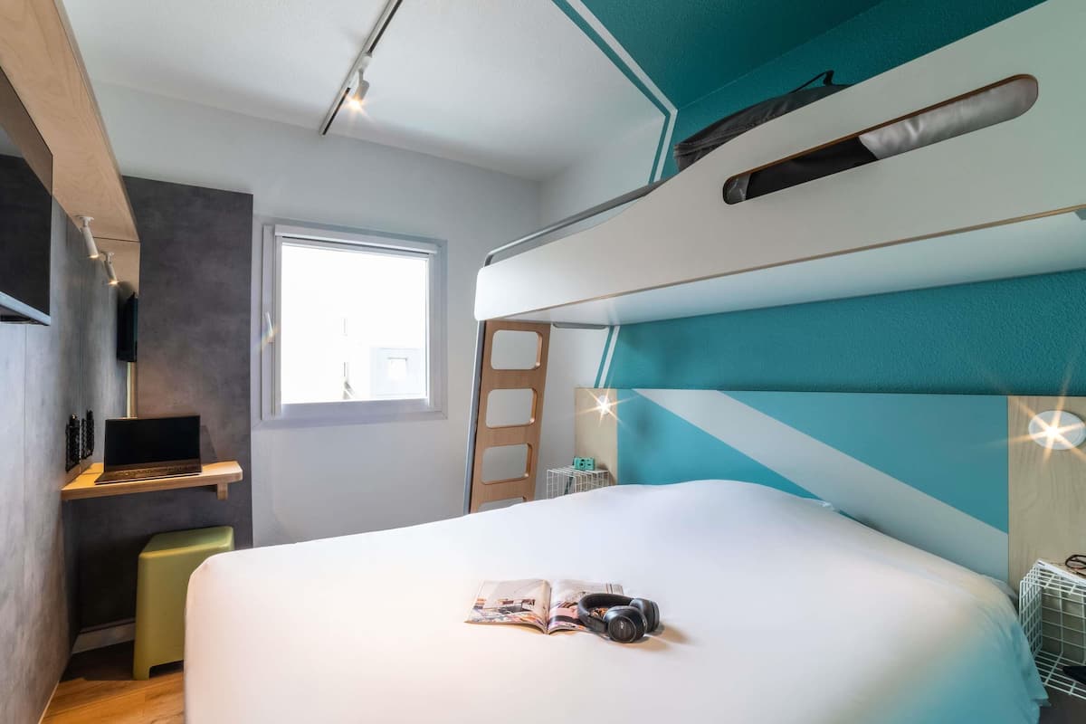 Quarto moderno com beliche, uma escrivaninha com um laptop, janela e um banquinho.