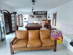 Uma sala de estar com um sofá de couro marrom, uma mesa de centro de madeira, uma mesa de jantar e uma bicicleta infantil rosa.