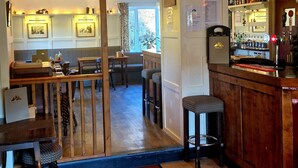 Uma área de bar com banquetas, balcão e vista para uma sala de jantar com mesas e cadeiras.