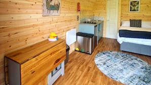 Uma cabana acolhedora com paredes de madeira, cozinha, cama e um tapete pequeno.