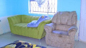 Quarto com sofá verde, poltrona bege e tapete estampado.