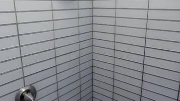 Um chuveiro no canto, com paredes e chão em azulejo.