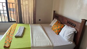 Uma cama com colcha verde e branca, um cobertor estampado e um travesseiro com padrão geométrico.