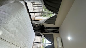 Quarto com cama, janela com cortinas, ar condicionado e vista para o verde lá fora.