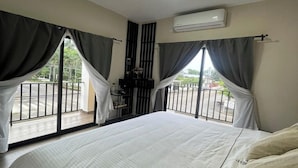 Quarto com uma cama grande, varanda com guarda-corpo e ar condicionado na parede.