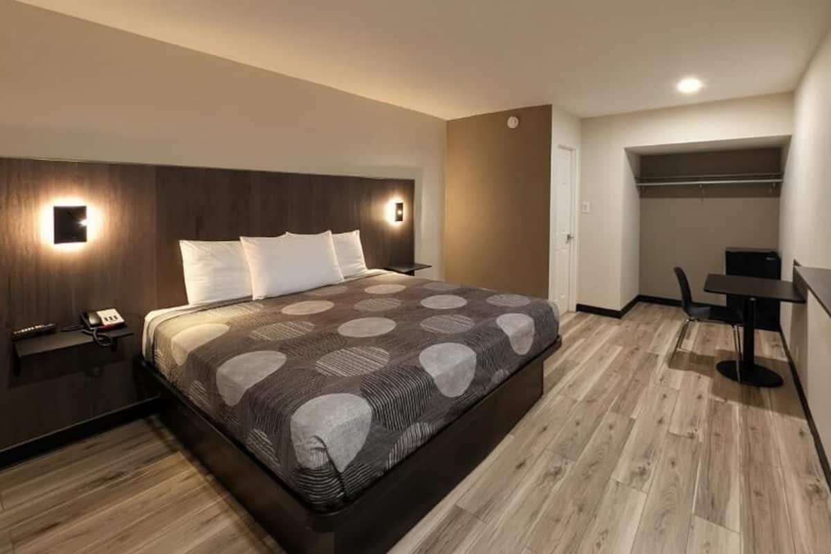 Quarto de hotel moderno com uma cama grande, mesas de cabeceira, escrivaninha e guarda-roupa.