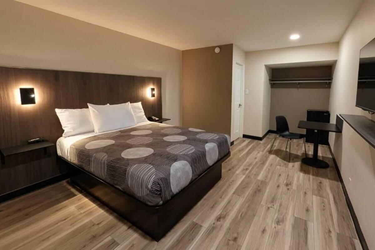 Quarto de hotel moderno com cama grande, escrivaninha, cadeira, guarda-roupa e televisão.