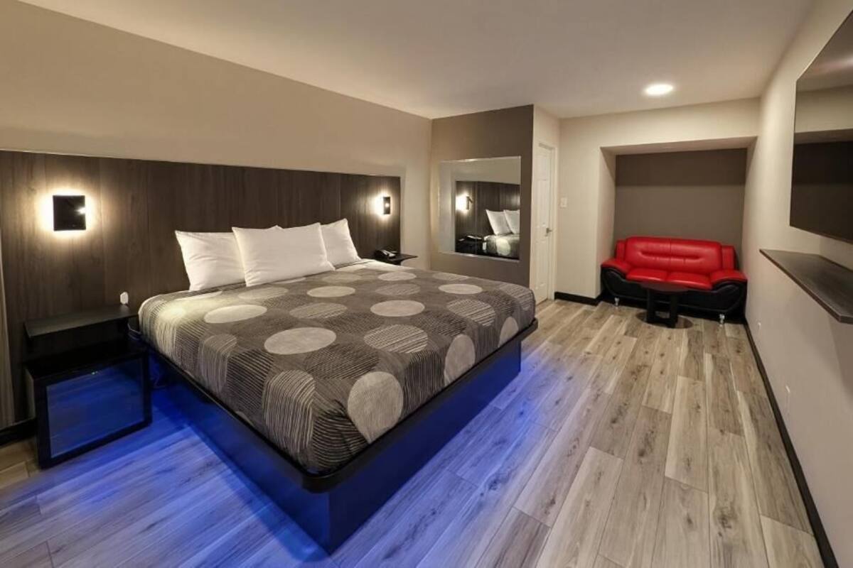 Quarto de hotel moderno com uma cama grande, um sofá vermelho, uma TV de tela plana e um espelho.
