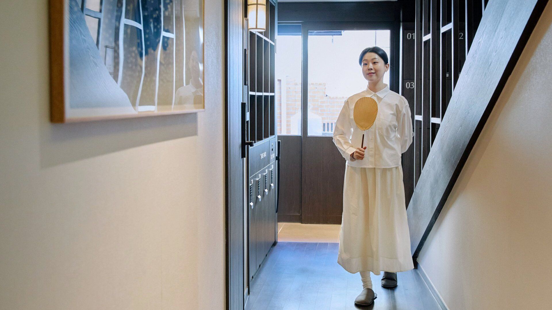 Uma pessoa vestida com traje tradicional em um corredor, com uma porta que dá para um quarto iluminado.