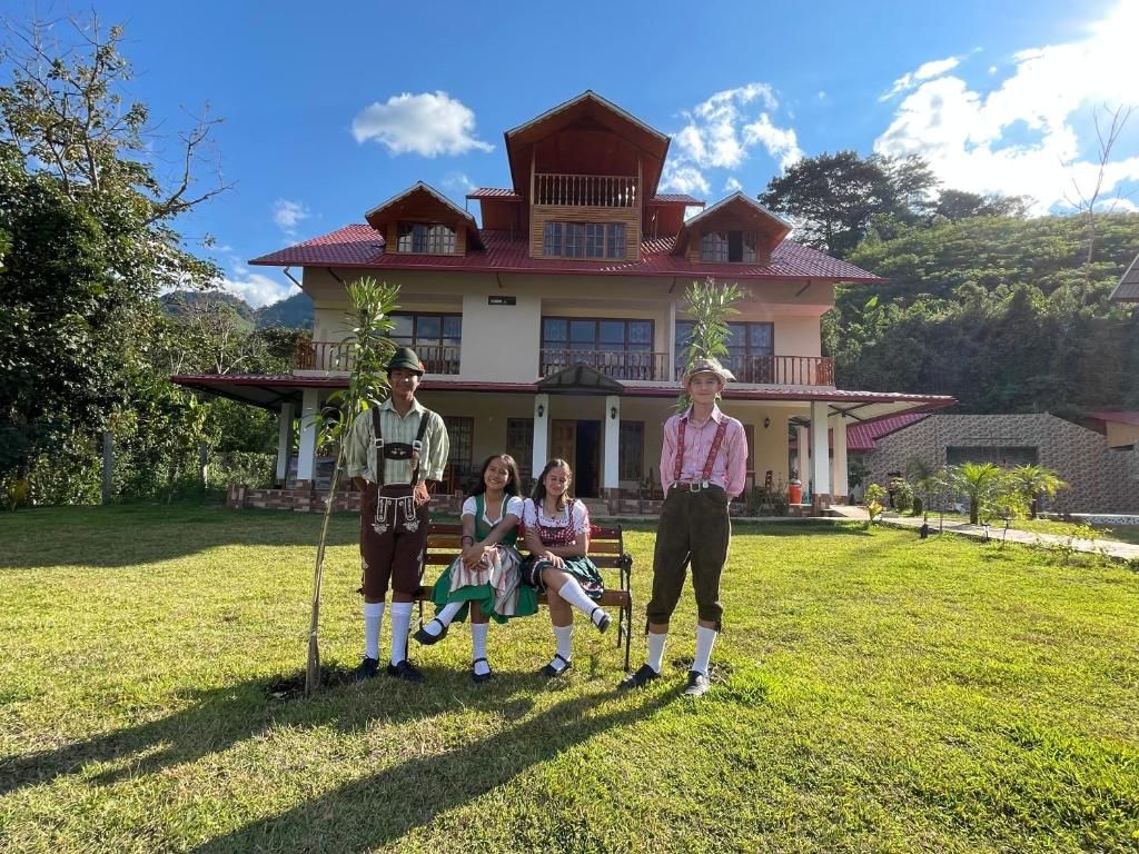 Um edifício grande com telhado vermelho e várias janelas, rodeado por vegetação.