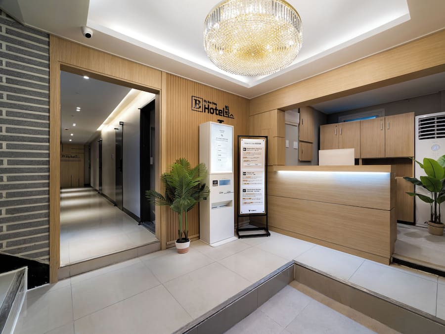 Uma área de recepção de hotel com design moderno, incluindo um balcão de atendimento, um candelabro e plantas em vasos.