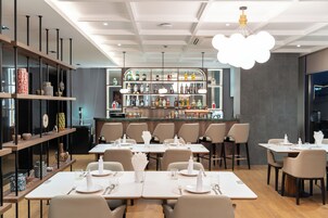 Um interior de restaurante moderno, com área de bar, mesas bem organizadas e diversos objetos decorativos em prateleiras.