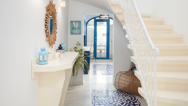 Um corredor com escada branca, soalho estampado e porta azul ao fundo.