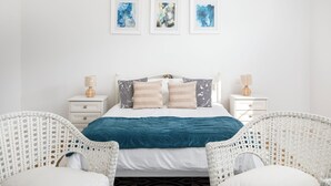 Quarto com uma cama, duas mesinhas de cabeceira, duas cadeiras de vime branco e três obras de arte emolduradas na parede.