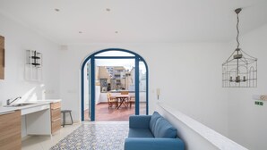 Cozinha moderna com área de jantar, um sofá azul e vista para o exterior por um arco.