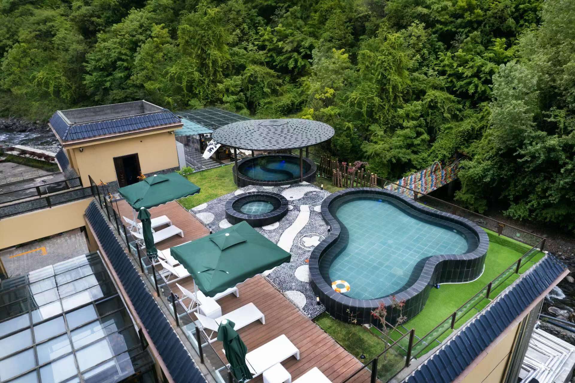 Uma área de piscina no terraço com várias banheiras de hidromassagem, espreguiçadeiras e um espaço de estar coberto.