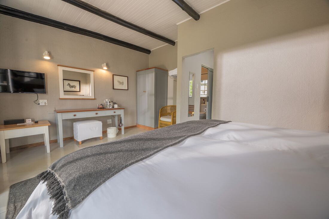 Quarto com cama, escrivaninha, cadeira, televisão presa à parede e guarda-roupa.