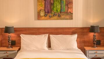Quarto de hotel com uma cama grande, duas mesas de cabeceira com luminárias, um ventilador de teto e uma pintura na parede.