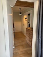 Um corredor com piso e teto de madeira, luminária pendente, espelho e cômoda de madeira.