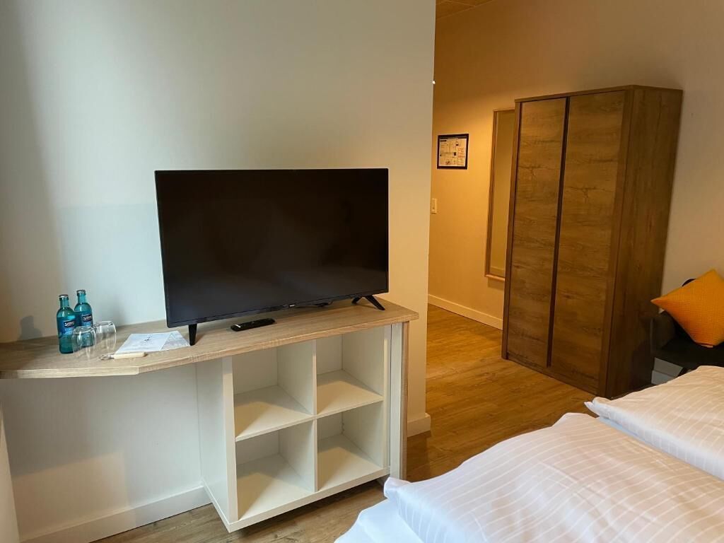 Quarto com televisão em um suporte, guarda-roupa e cama.