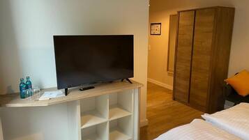 Quarto com televisão em um suporte, guarda-roupa e cama.