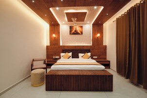 Quarto moderno com cabeceira de madeira, cama com roupa de cama branca e amarela, mesa de cabeceira, um banco de madeira e um ventilador de teto.