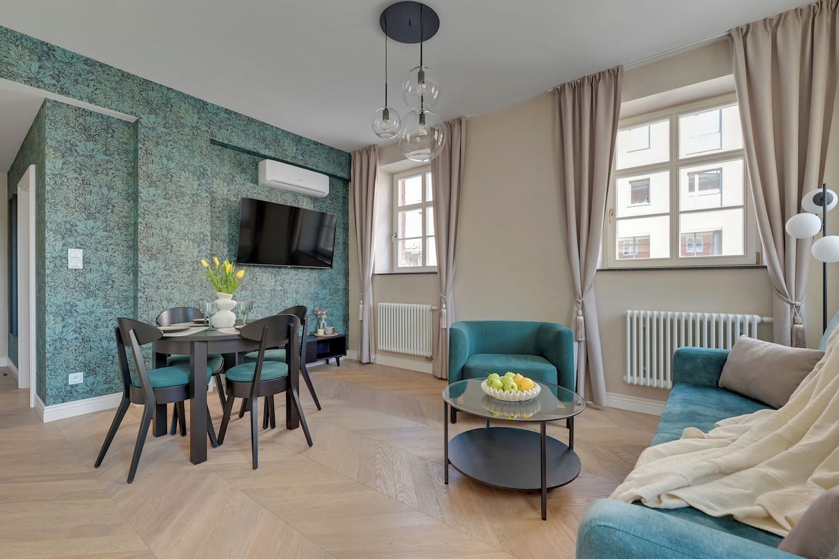 Uma sala de estar moderna com área de jantar, um sofá verde-água e uma TV na parede.