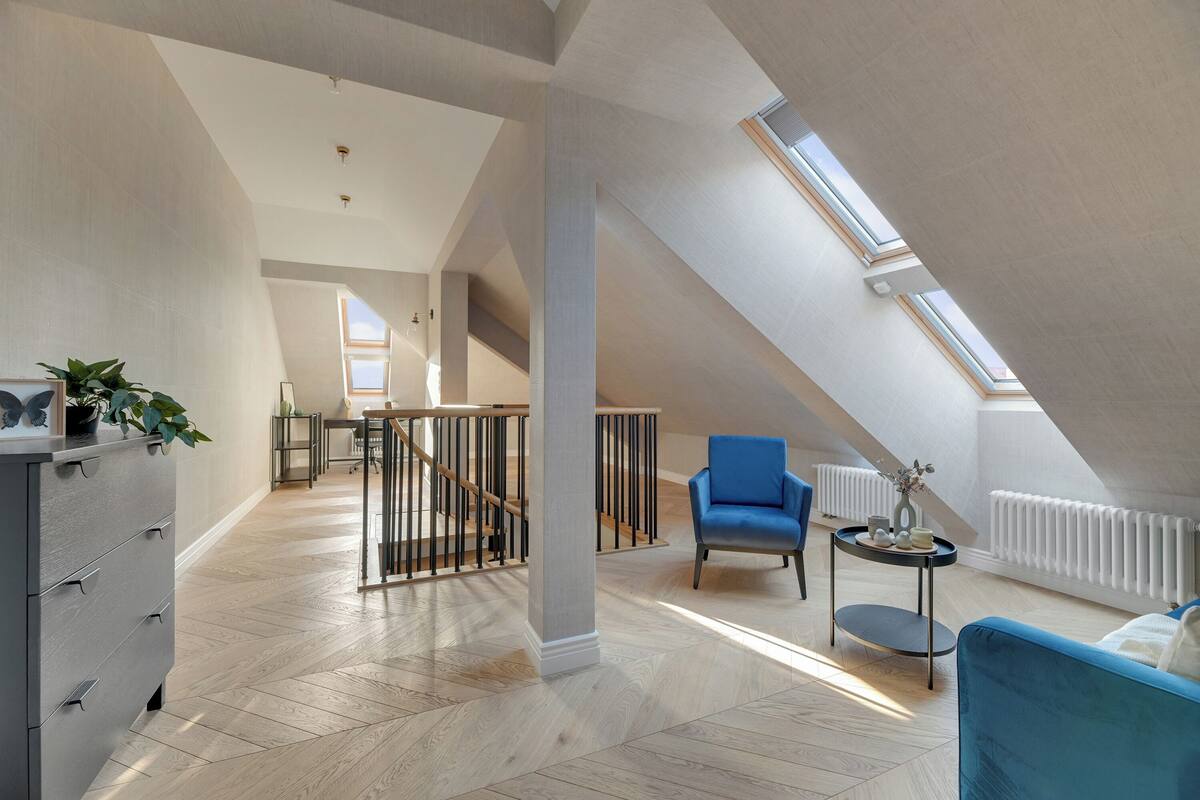 Um loft espaçoso com pé-direito alto, uma escada de madeira, uma poltrona azul e uma área de refeições.