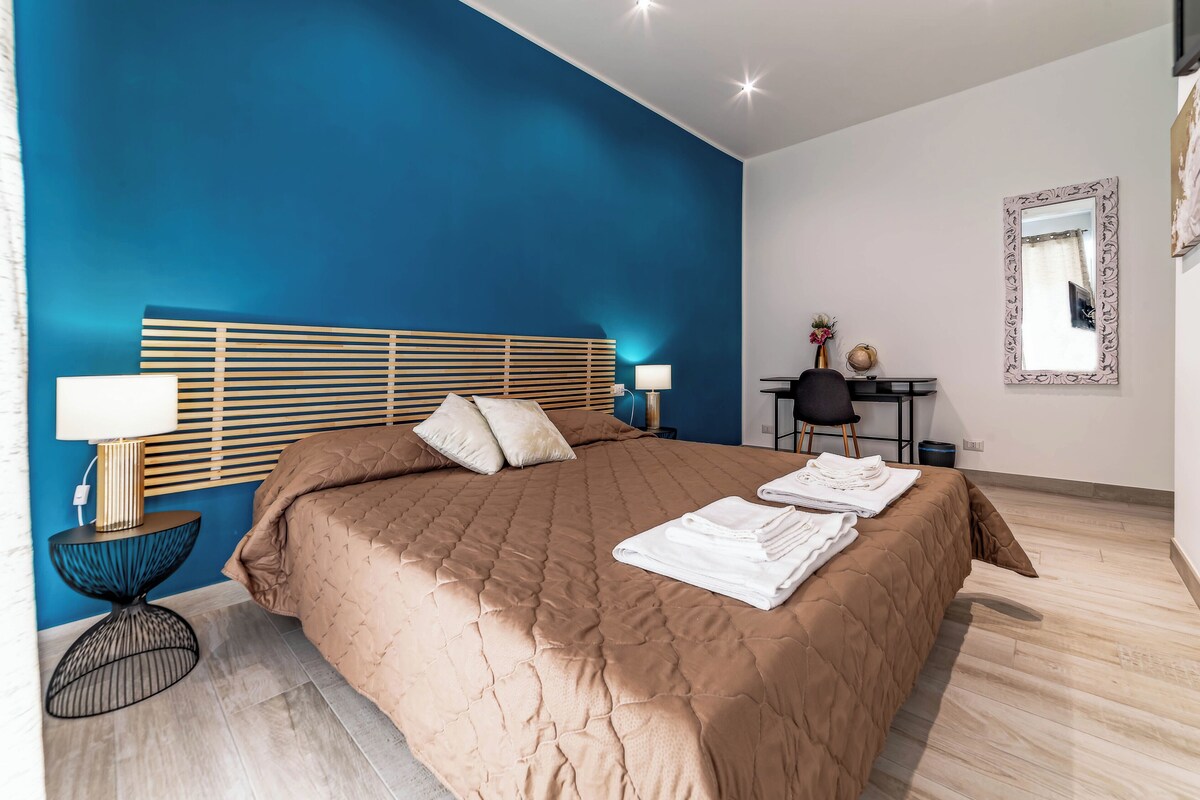 Quarto com uma cama grande, duas mesas de cabeceira, uma escrivaninha e um espelho na parede.