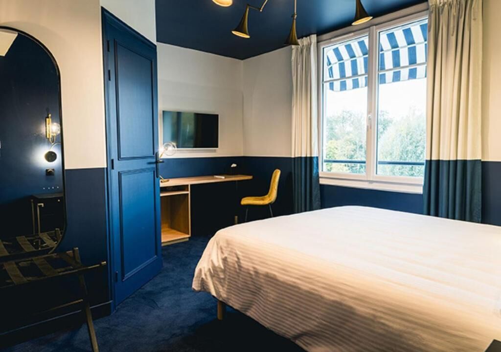 Quarto com cama, escrivaninha, cadeira, televisão e janela com cortinas.