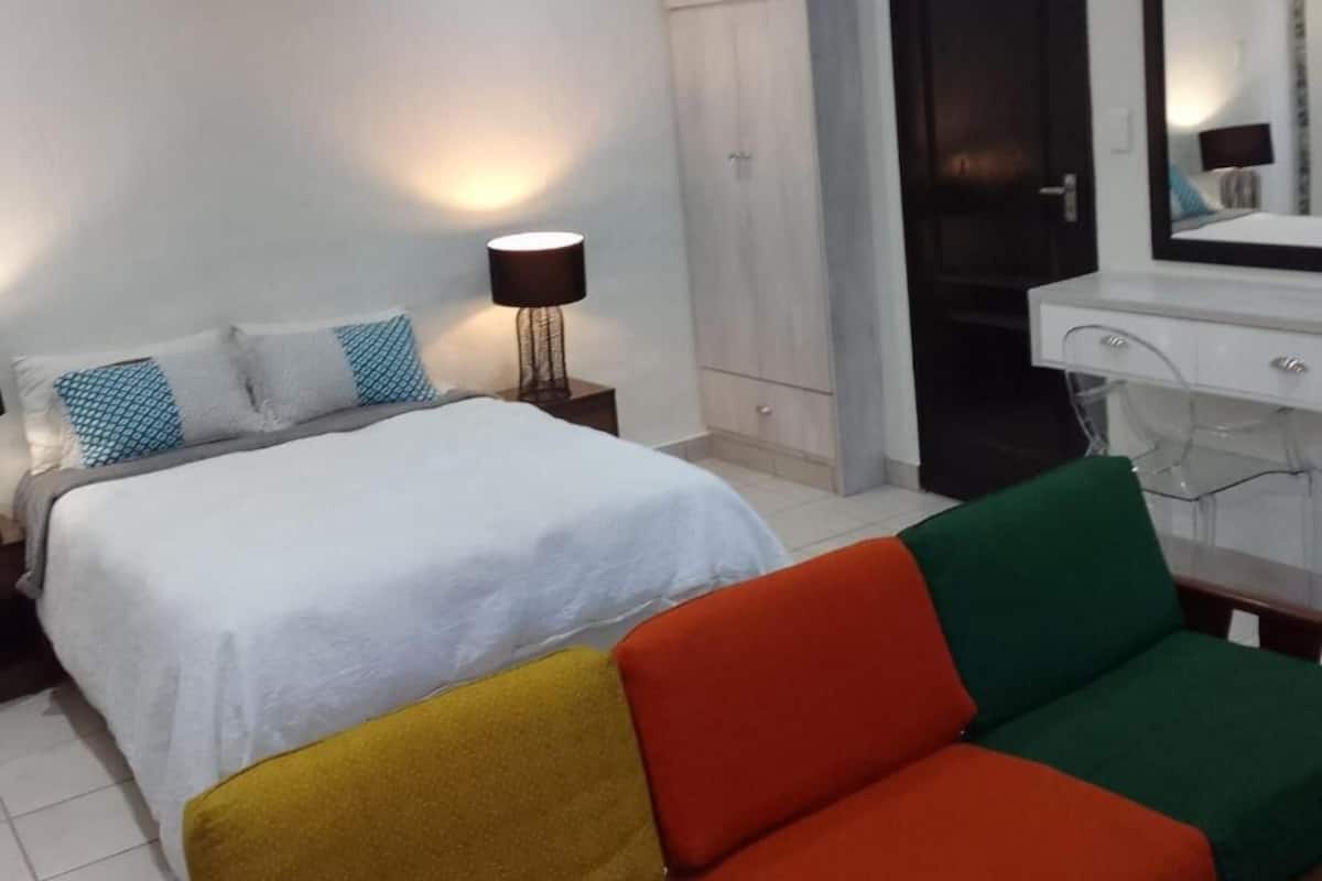 Um quarto com uma cama, mesa de cabeceira com luminária, guarda-roupa e espelho.