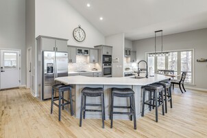 Cozinha moderna com ilha central, banquetas, um relógio e uma janela grande.
