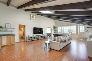 Uma sala de estar ampla com uma televisão grande, piso de madeira, um sofá e uma mesa de jantar.