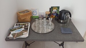Uma mesa com uma bandeja de copos, uma cafeteira, uma caixa de chá, um livro com tema de panda, uma caixa de madeira e uma revista.