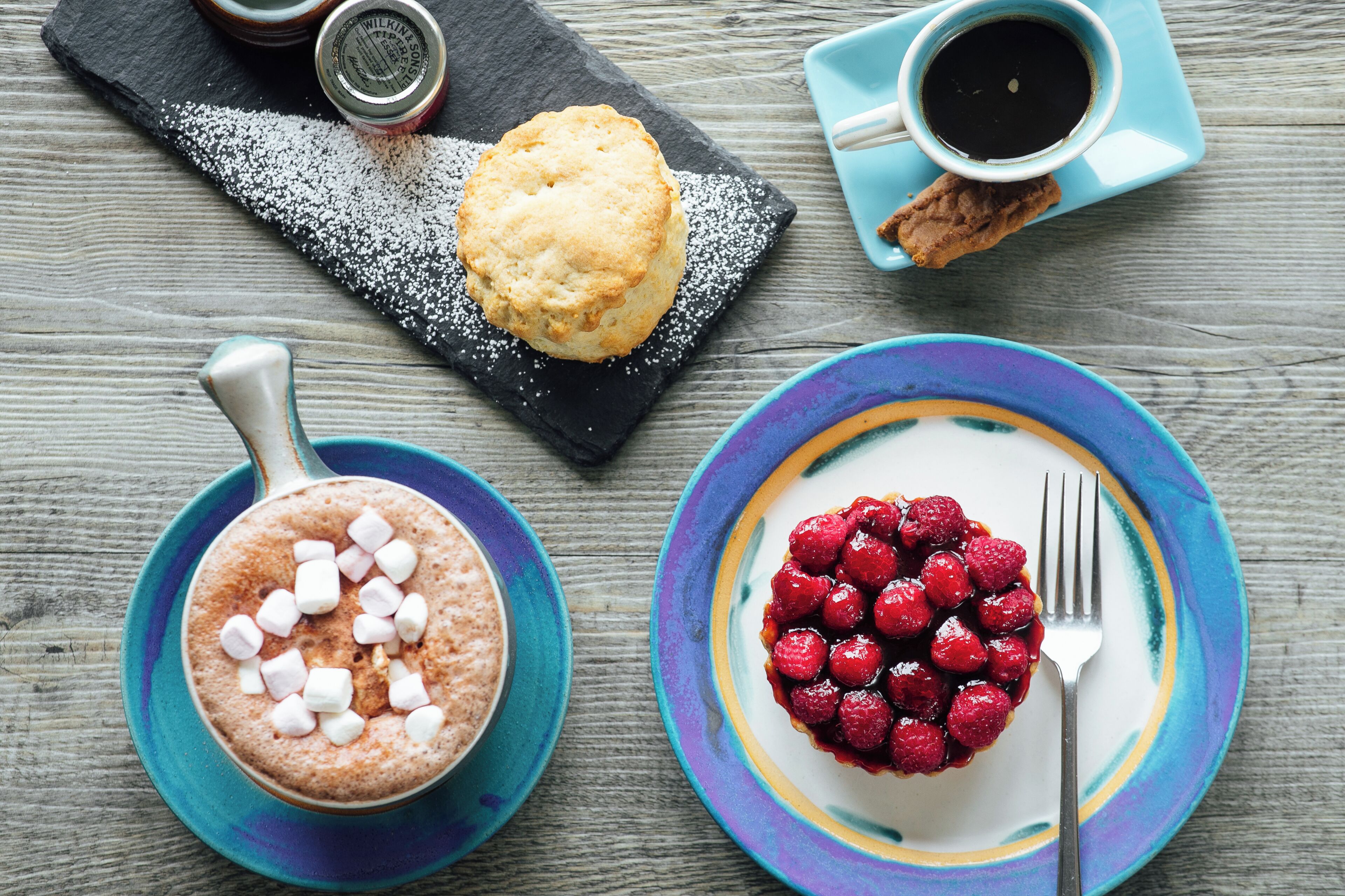 Uma mesa de sobremesas com uma bebida de chocolate, uma torta de frutas vermelhas e um biscoito.