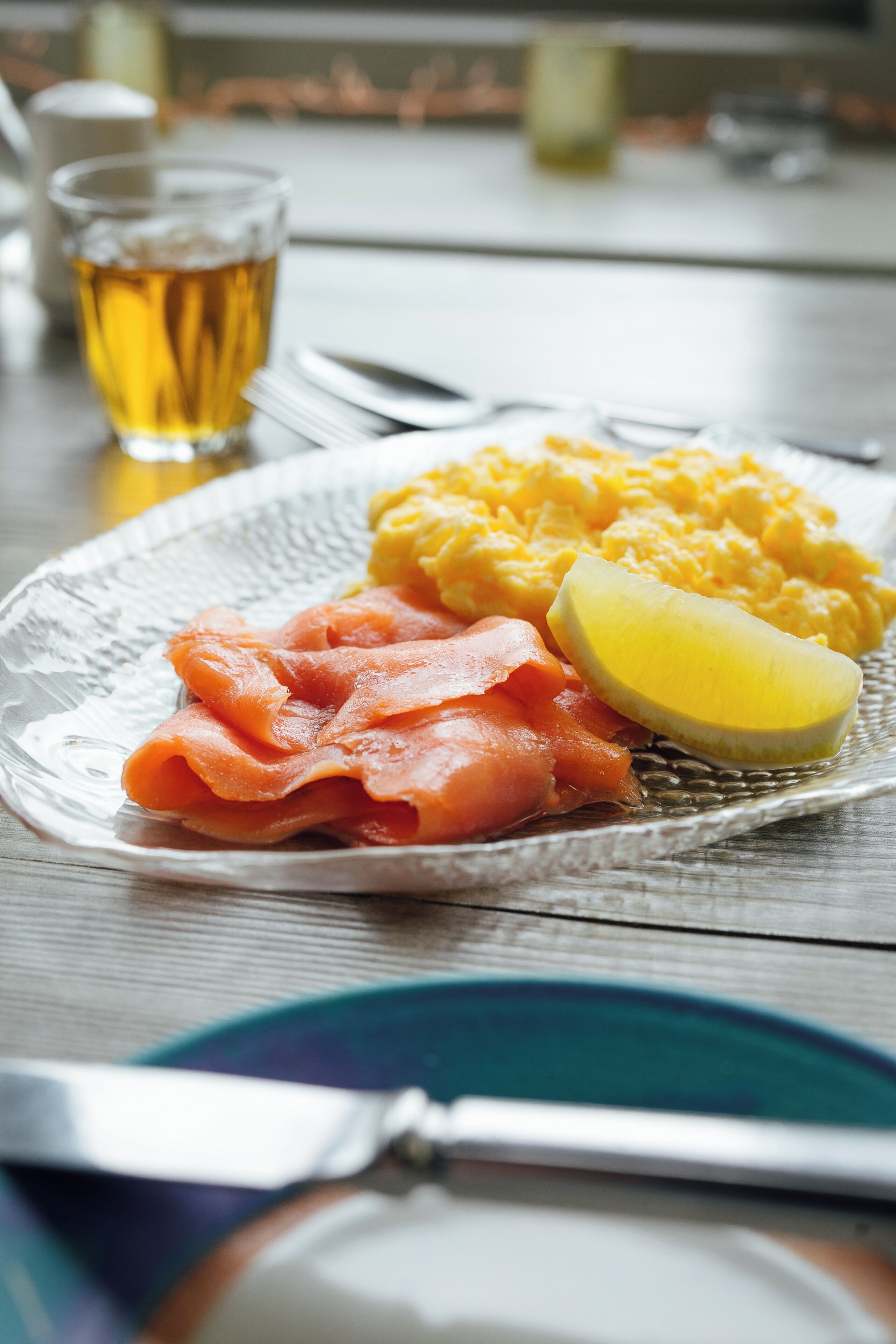 Prato com salmão, ovos mexidos e uma fatia de limão em um prato de vidro texturizado.