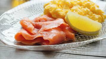 Prato com salmão, ovos mexidos e uma fatia de limão em um prato de vidro texturizado.