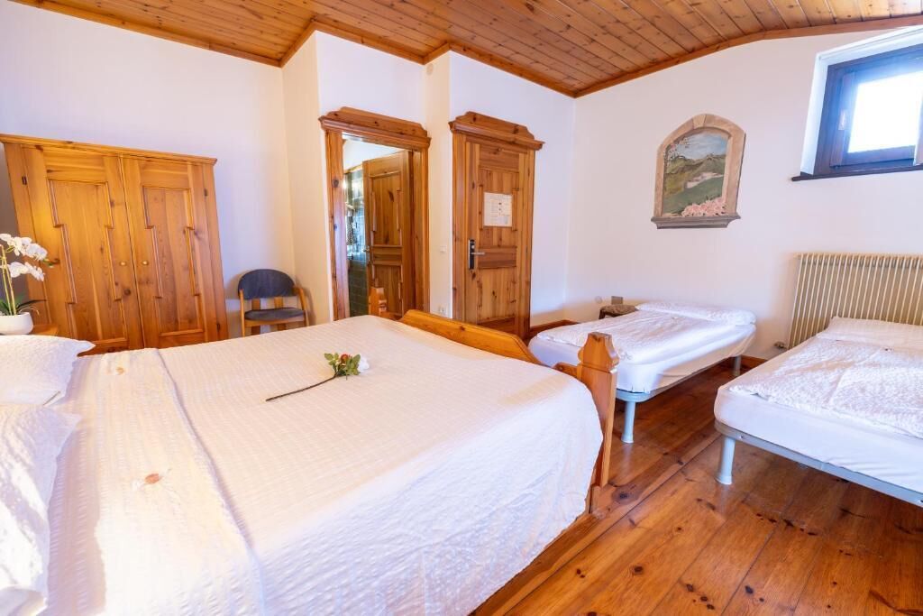 Quarto com piso de madeira, duas camas, uma cadeira e um guarda-roupa de madeira.